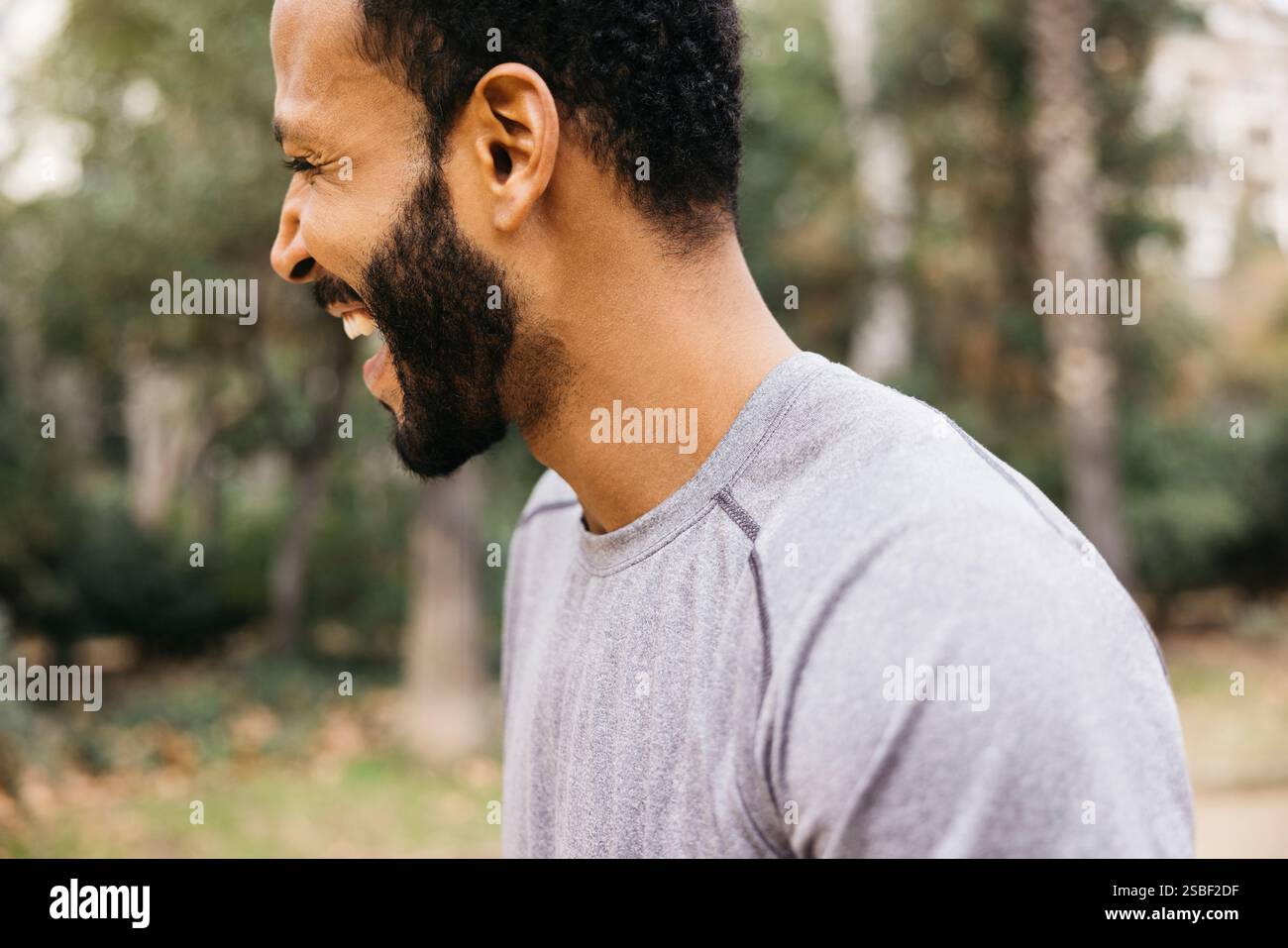 Side profile of a cheerful man laughing in an outdoor park with lush ...