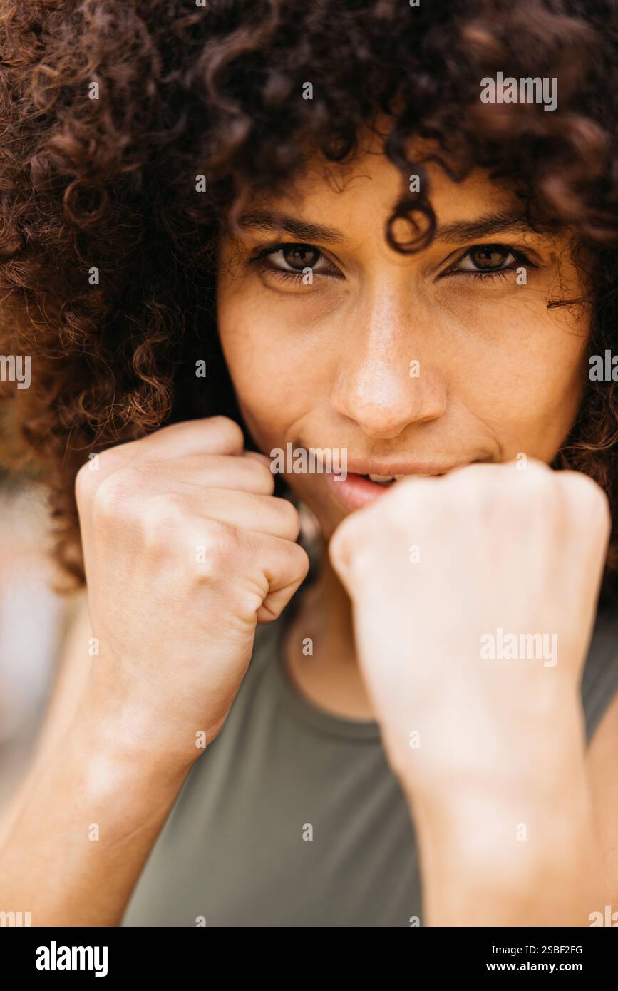 A focused young woman with curly hair posing in a fighting stance ...