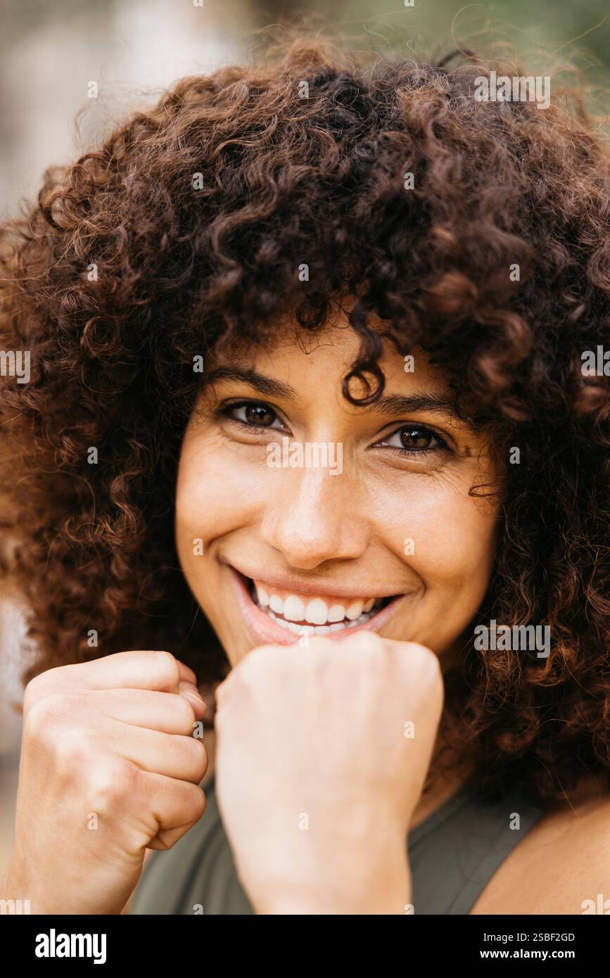 A cheerful woman with curly hair raising her fists in a boxing stance ...
