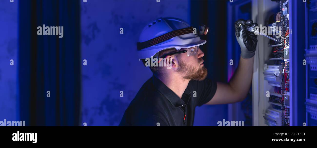 A male electrician works in a switchboard in overalls against the ...