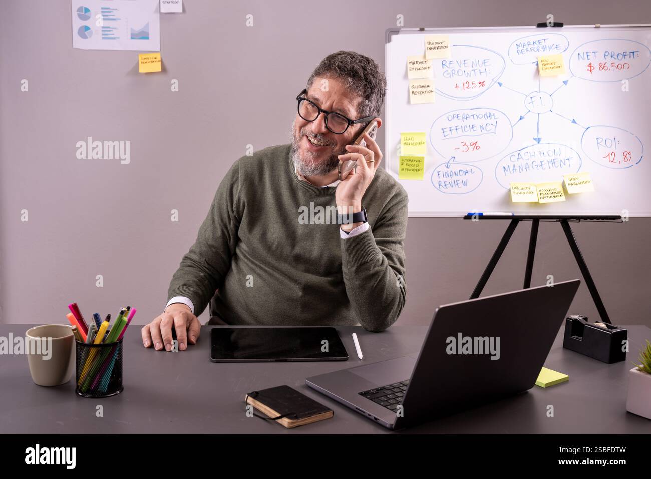 Senior businessman sitting at office desk while talking on the phone ...