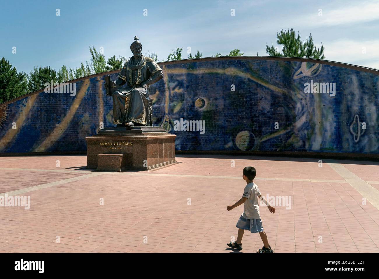 A young boy walks past a large statue of a seated figure against a ...