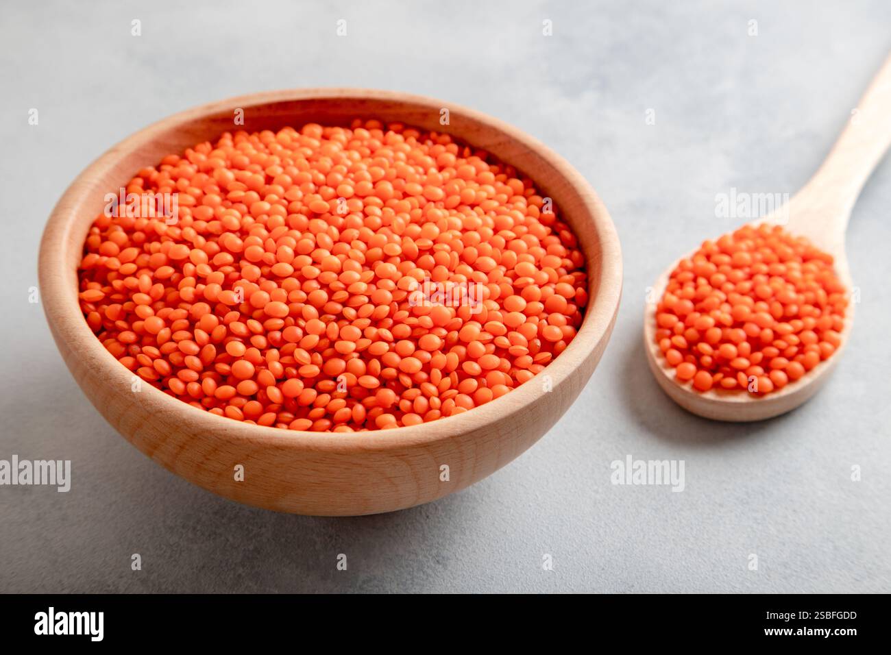Red lentil grains in a wooden bowl on light blue background. Top view ...