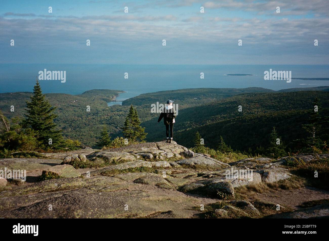 A hiker stands atop a rocky summit overlooking Acadia National Park ...
