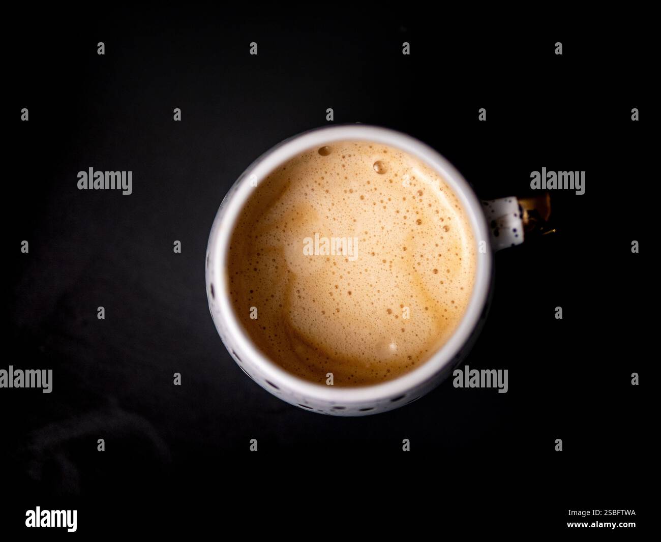 A white coffee cup with foam on top. The foam is brown and the cup is ...
