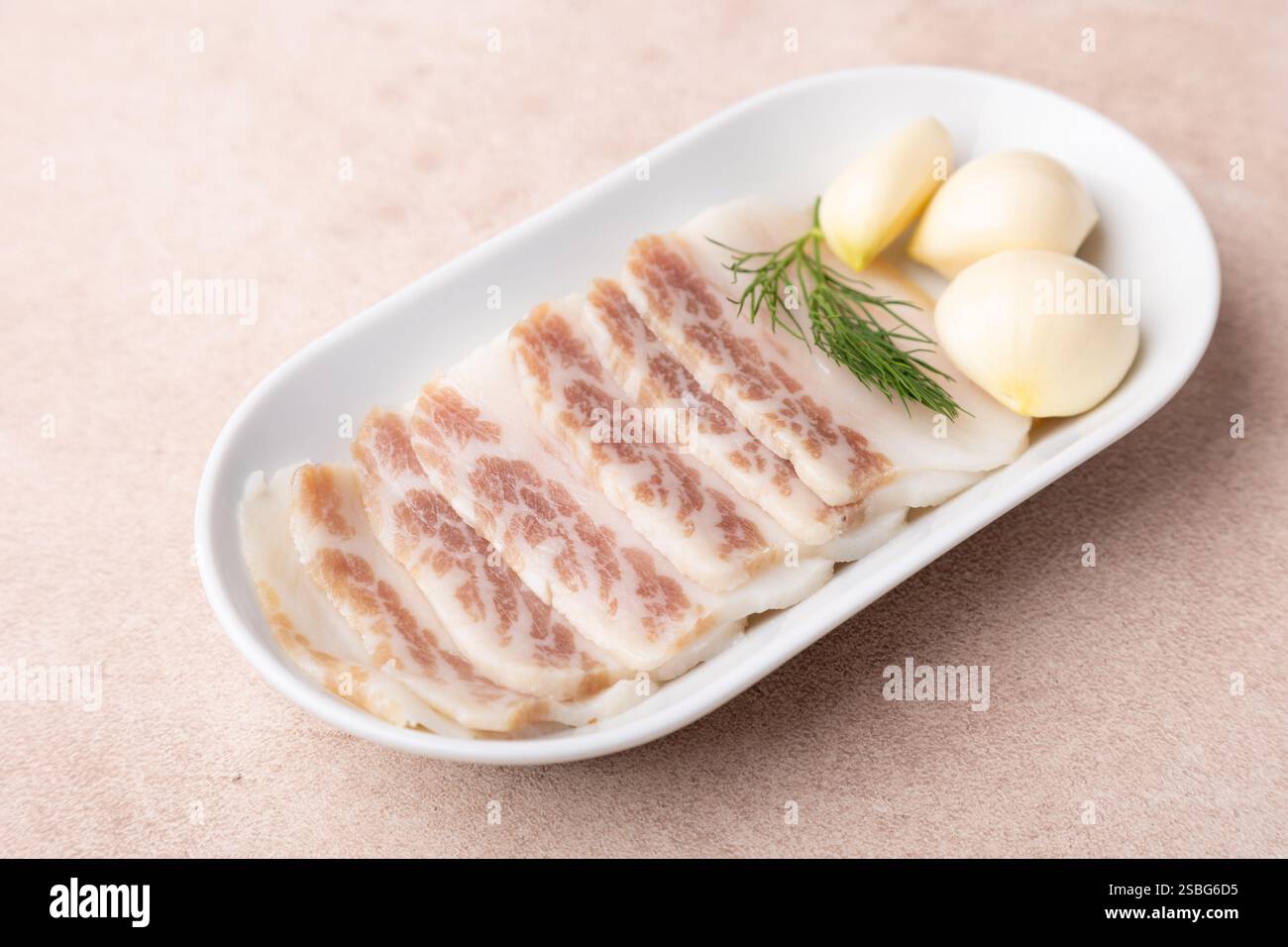Homemade salted pork lard, sliced, with garlic cloves on a white plate ...