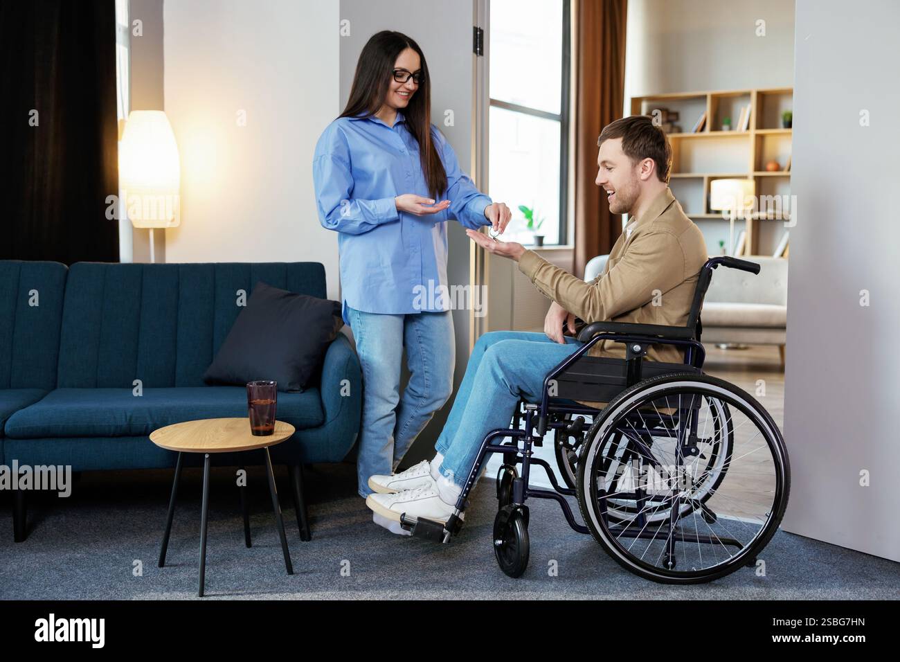 Man in wheelchair extend her hand palm up to side. Woman giving key ...