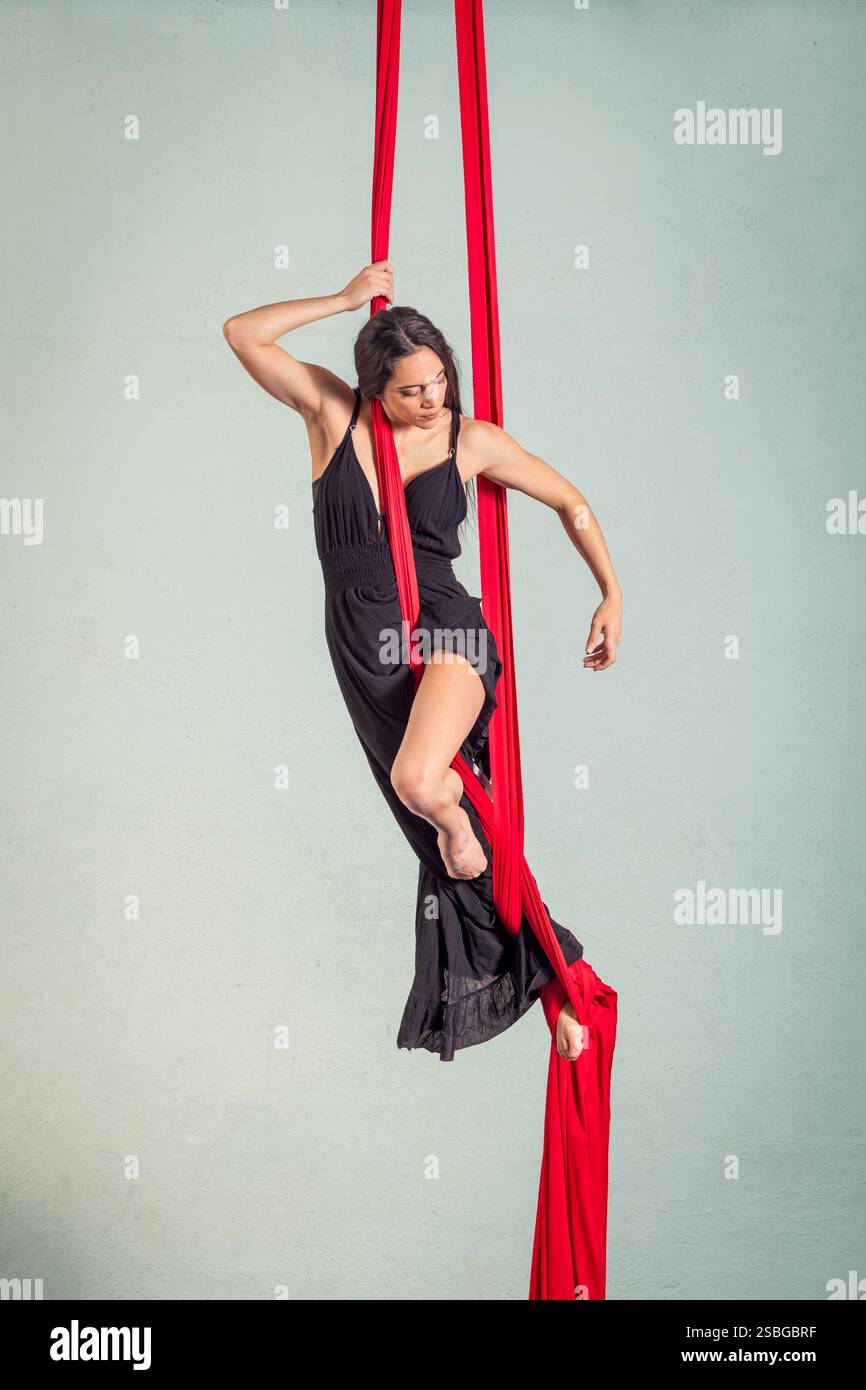 Young woman acrobat performing aerial dance on red silks in studio ...