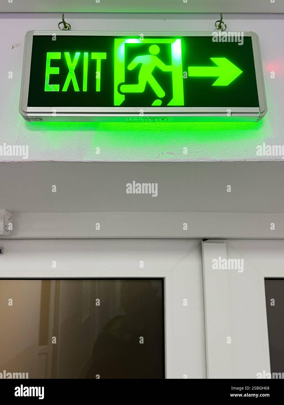 Green illuminated exit sign displaying a running figure with an arrow ...