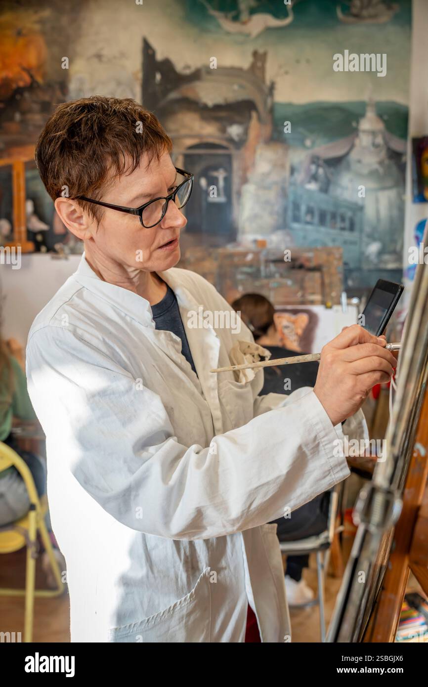 A smiling mature woman with short hair and glasses paints a picture ...