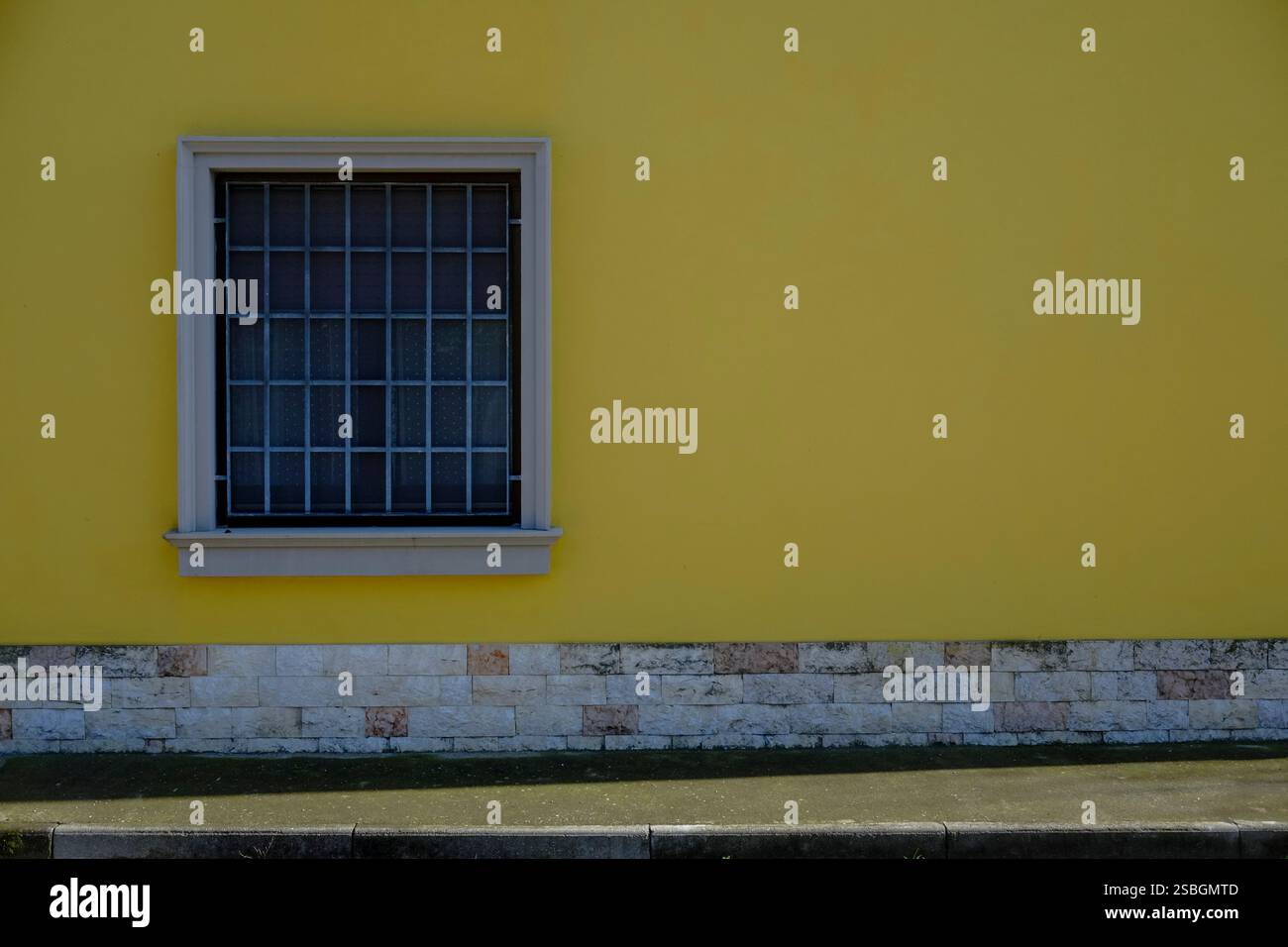 A single window with a gridded pane sits in a bright yellow wall, above ...