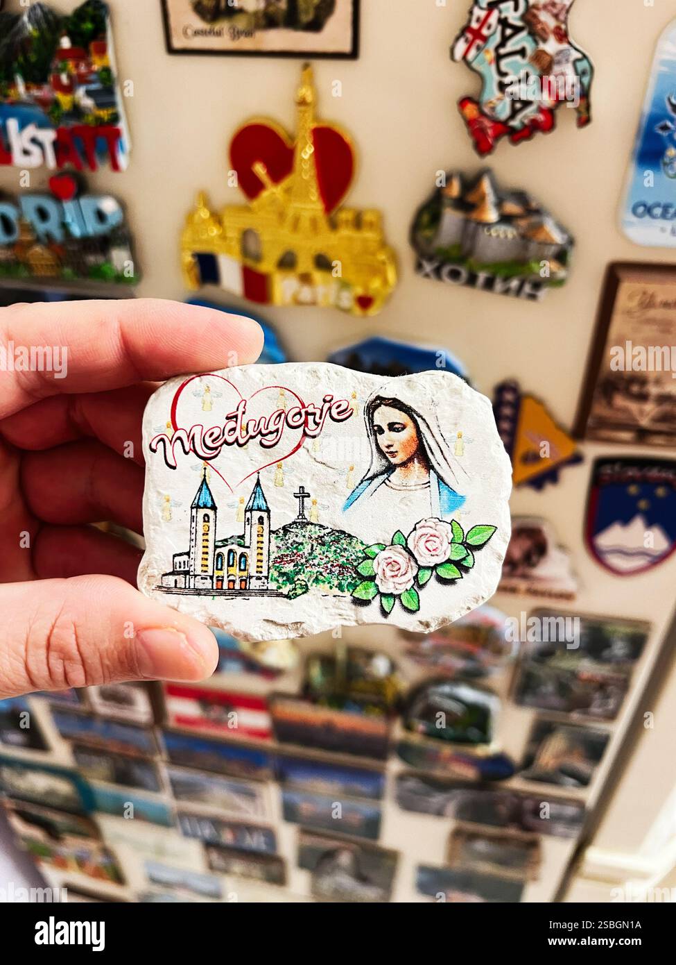A hand holds a colorful souvenir magnet displaying Medjugorje scenery ...