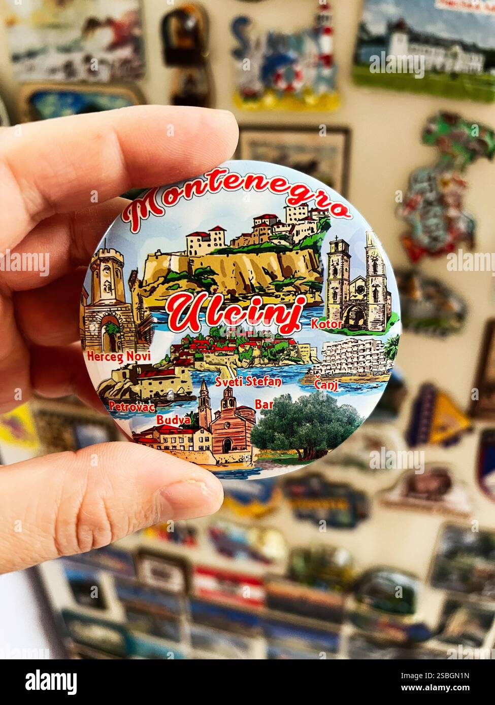 A hand holding a souvenir magnet displaying various notable locations ...
