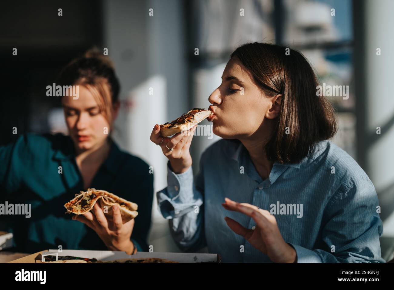 Two women enjoying pizza during a casual lunch break Stock Photo - Alamy