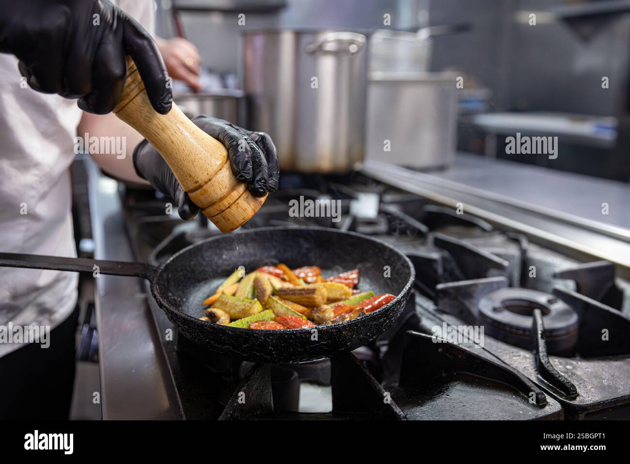Chef adding spices to grilled vegetables in frying pan on gas stove ...