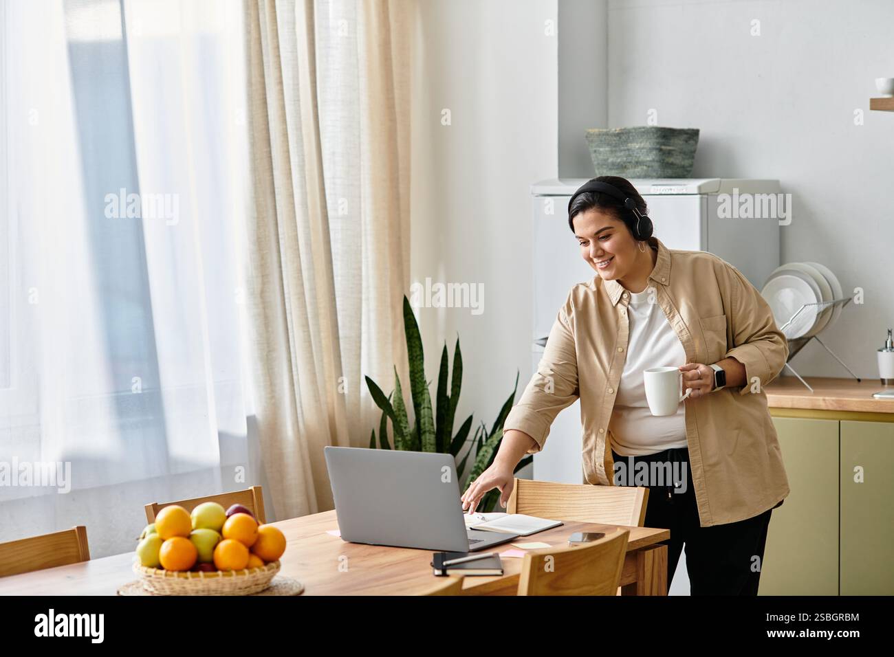 Bright daylight fills the cozy kitchen as a young plus size woman sips ...