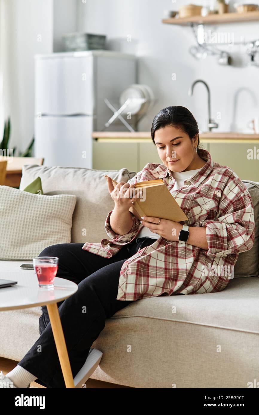 A young plus sized woman relaxes on the sofa, deeply engaged in her ...