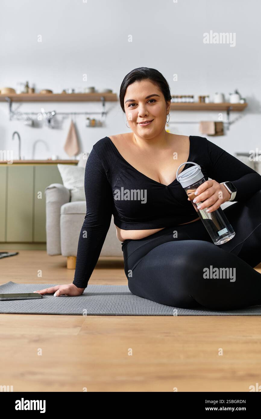 A young plus sized woman relaxes with a water bottle after completing ...
