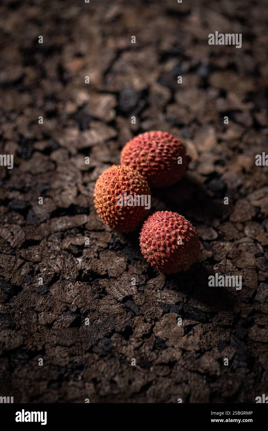Three lychees resting on cracked dark surface, a study in contrast ...