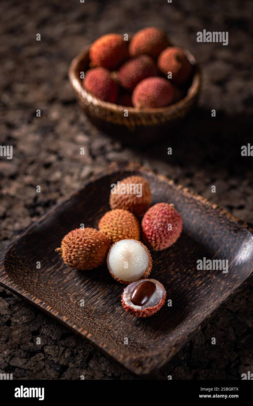 Fresh lychees displayed on rustic wooden tray, showcasing ripe and open ...