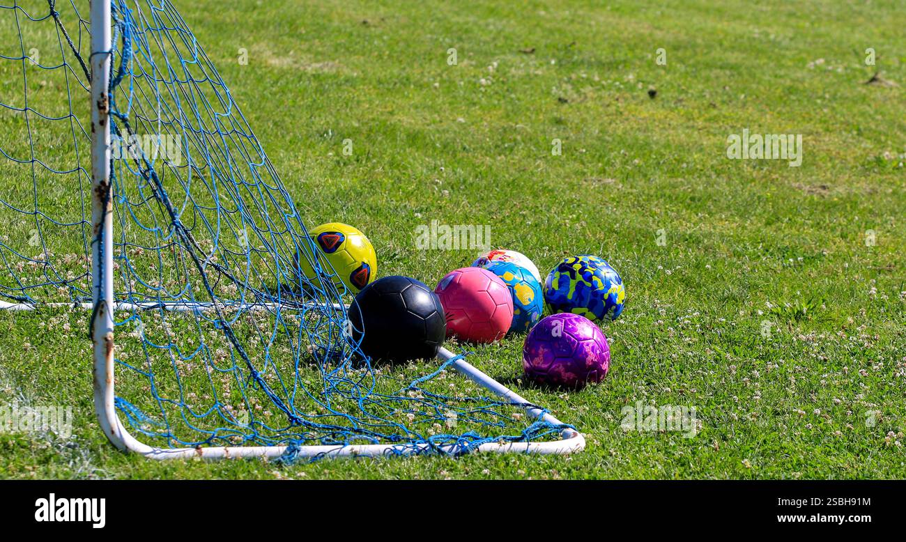 A variety of soccer balls in different colors gather beside the goal ...