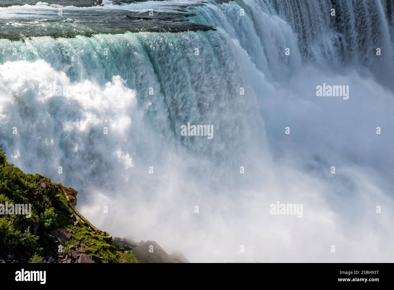 Water flows vigorously over the cliffs, creating mist and vibrant ...