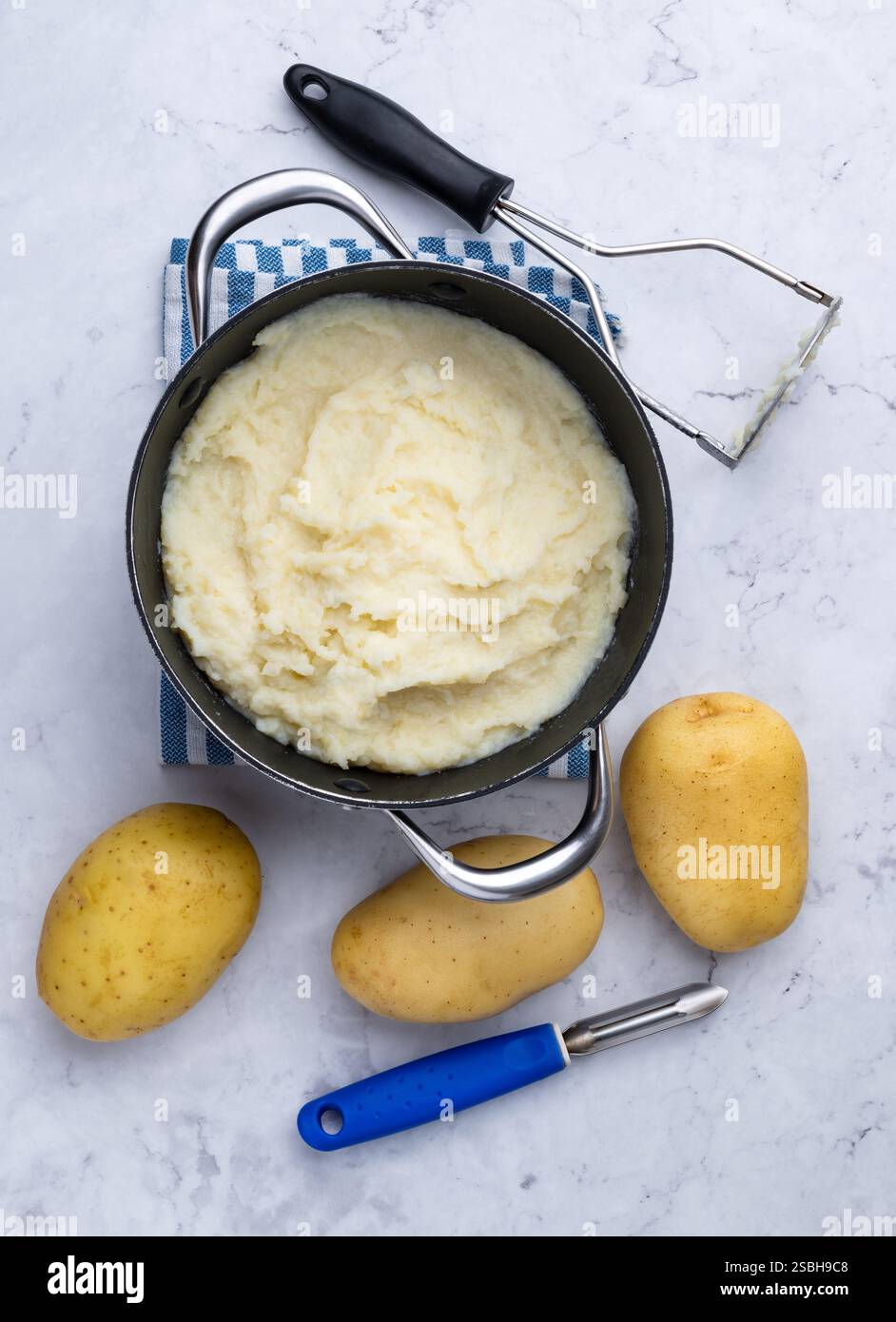 Mashed potatoes in a pan with potatoes and utensils over white marble ...