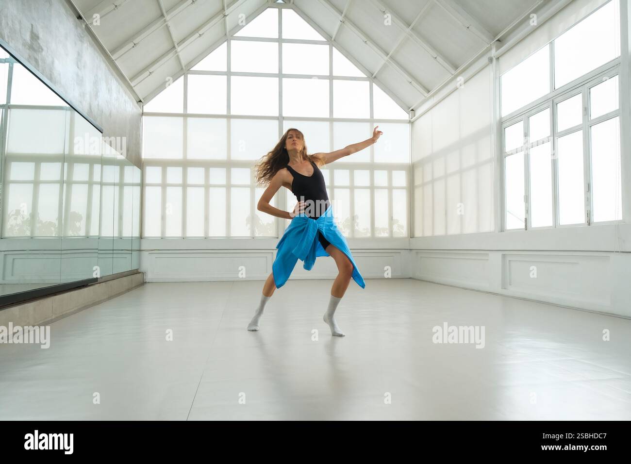 A woman performs a contemporary dance in a bright studio with large ...