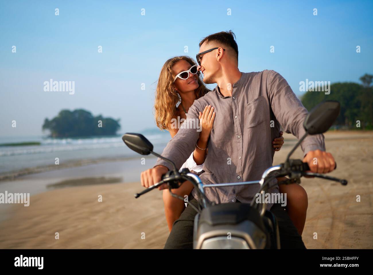 Couple rides motorcycle on beach. Man drives while woman embraces him ...