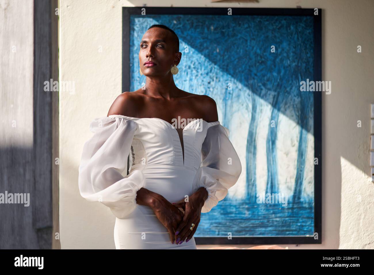 Ethnic black person in white bridal dress stands in villa with art ...