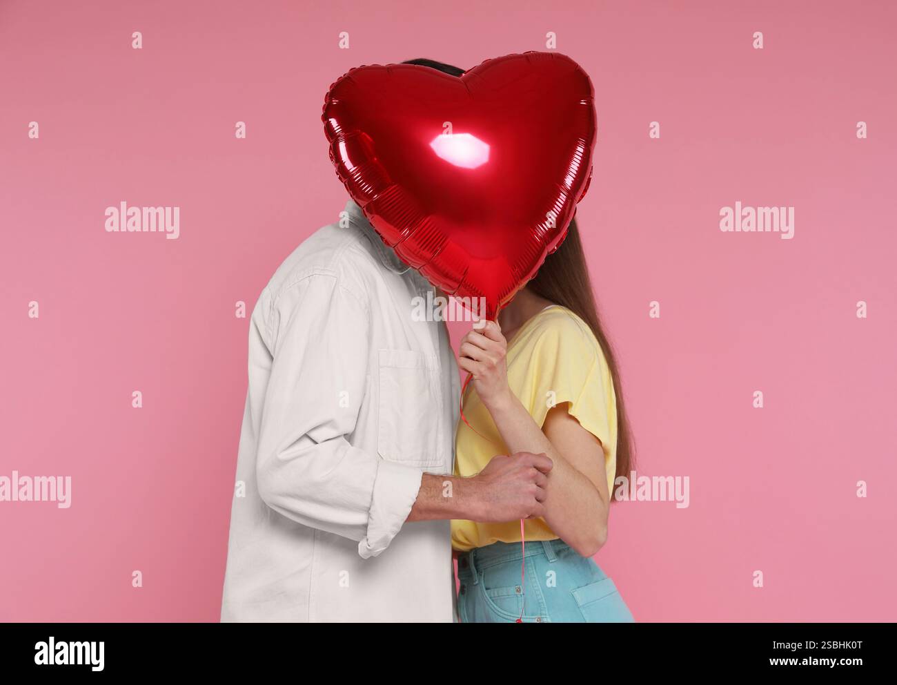 Lovely couple kissing behind heart shaped balloon on pink background ...