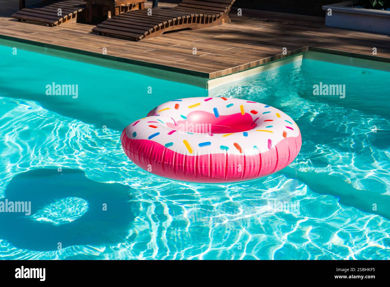 Pink donut inflatable float in turquoise swimming pool with wooden deck ...