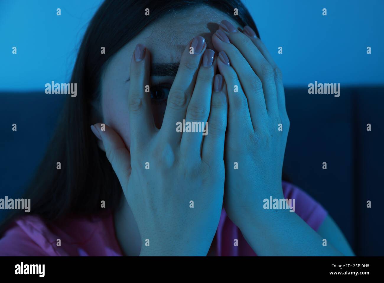 Fear of darkness. Scared young woman on bed and hiding her face in room ...