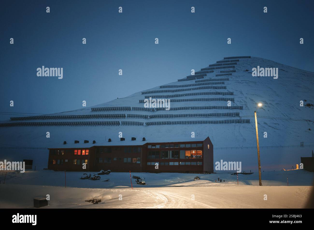 Snowy arctic mountain behind building in the polar night, Longyearbyen ...