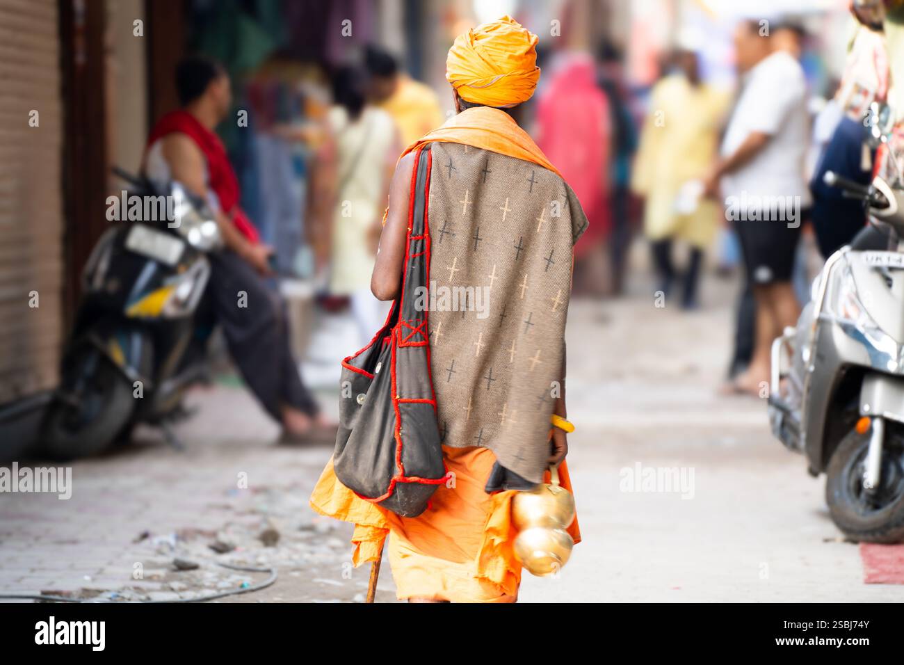 Rear shot of hindu holy man sadhu priest with bags walking in the busy ...