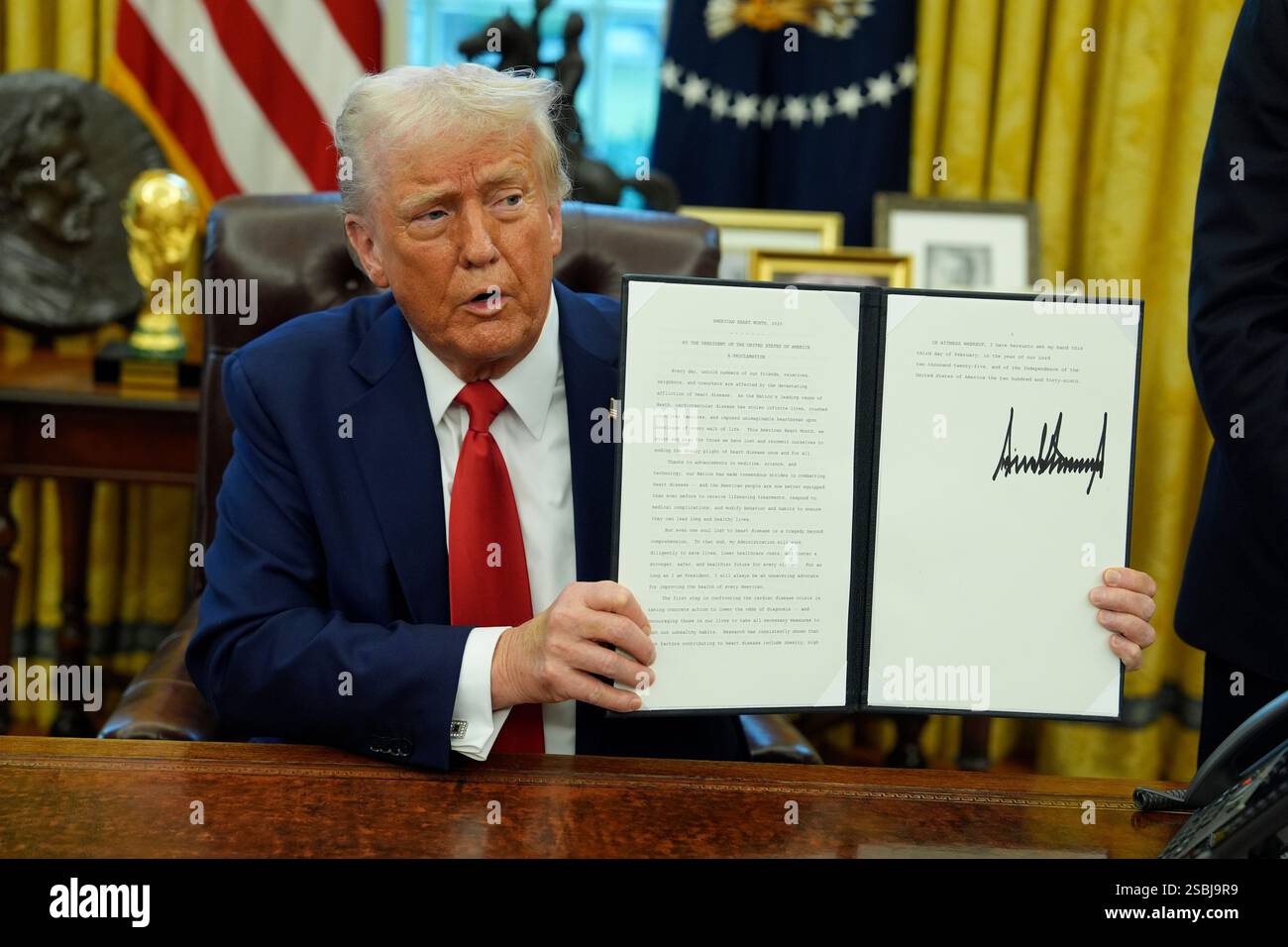 President Donald Trump holds up a signed executive order in the Oval ...