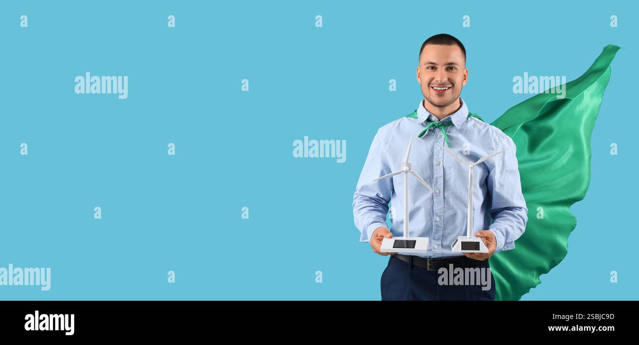 Male engineer in superhero cape holding wind turbine models on light ...