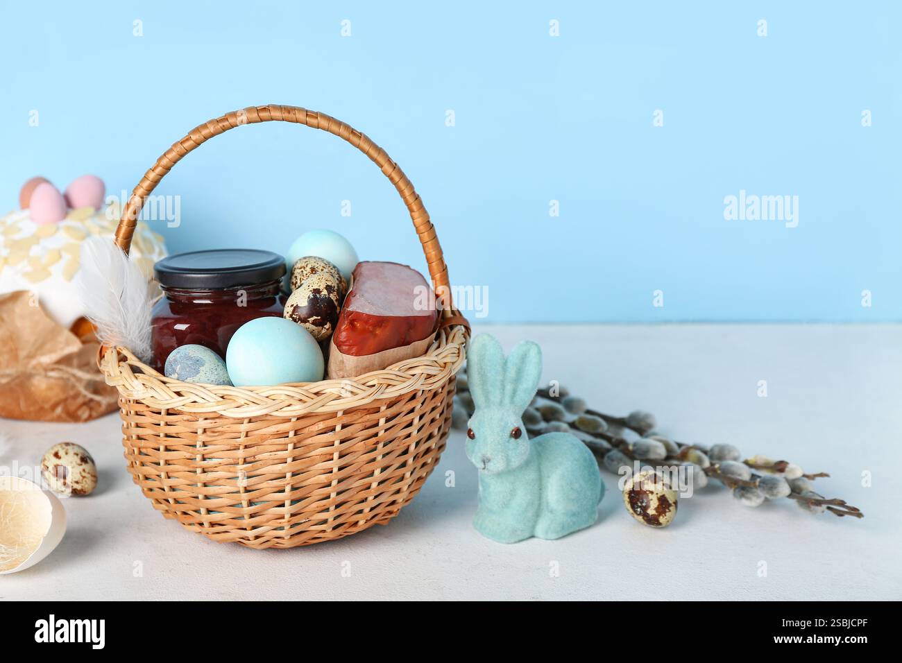 Basket with Easter eggs, ham and bunny on grey table against blue ...