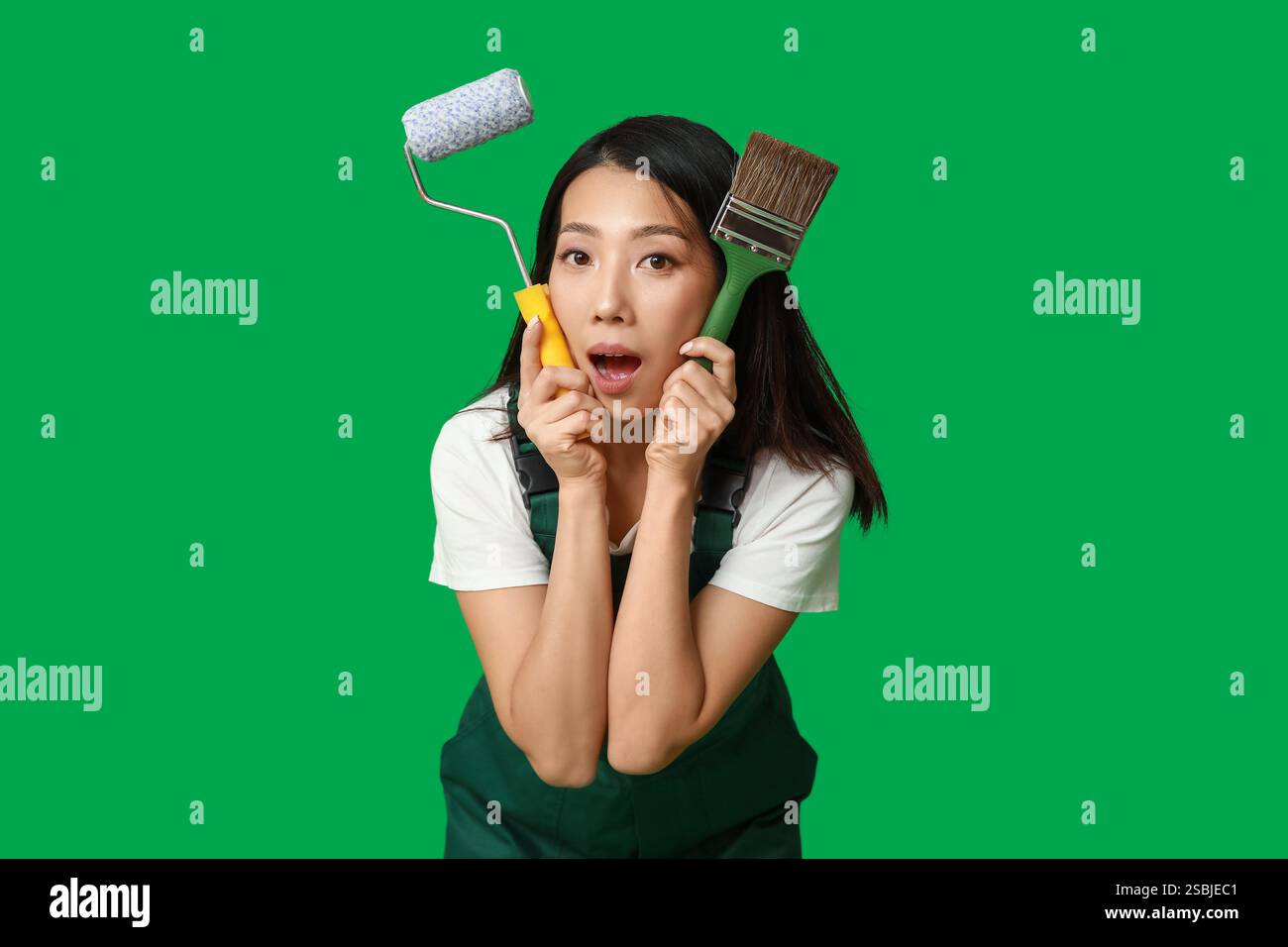 Female Asian shocked painter with roller and brush on green background ...