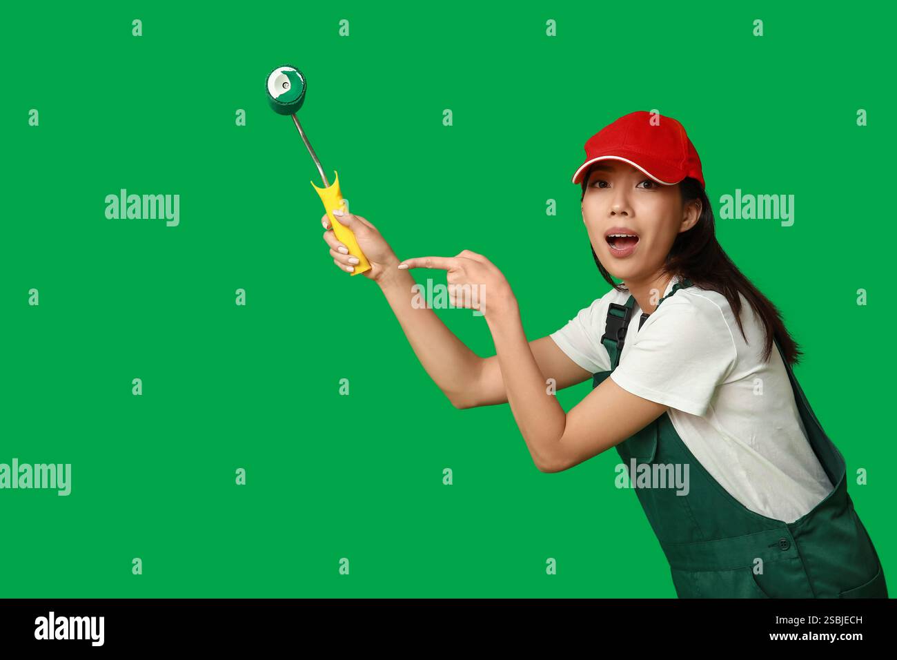 Female Asian shocked painter pointing at roller on green background ...