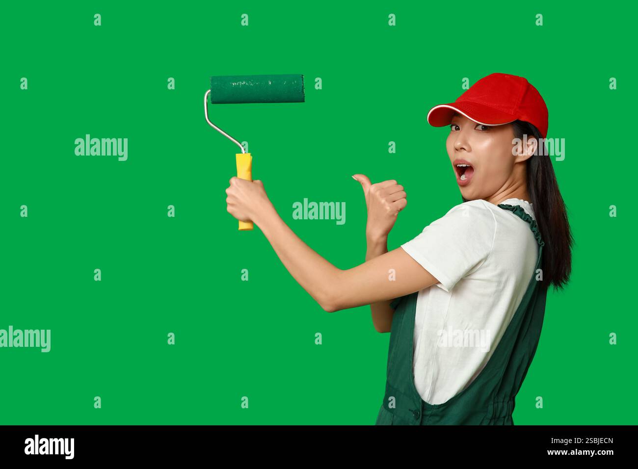 Female Asian shocked painter pointing at roller on green background ...