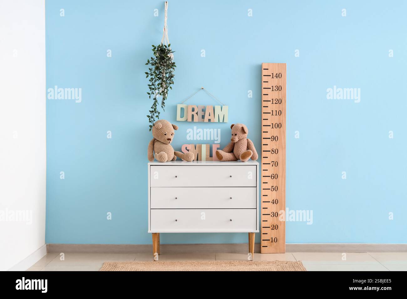 Wooden stadiometer and chest of drawers with plush toys near blue wall ...
