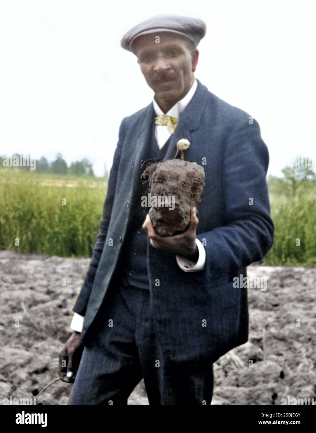 Carver, standing in field, probably at Tuskegee, holding piece of soil ...