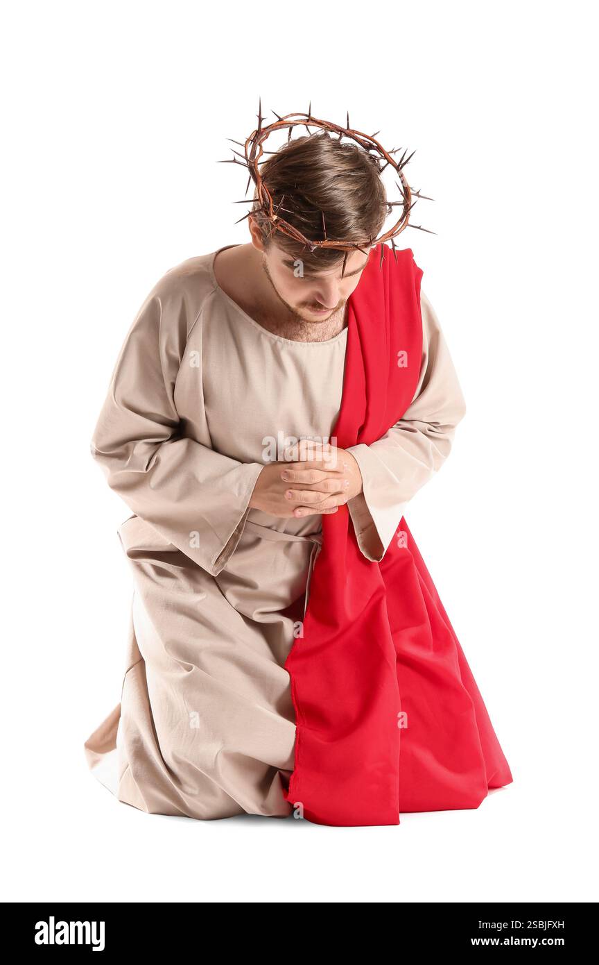 Man in Jesus robe and crown of thorns praying on knees against white ...
