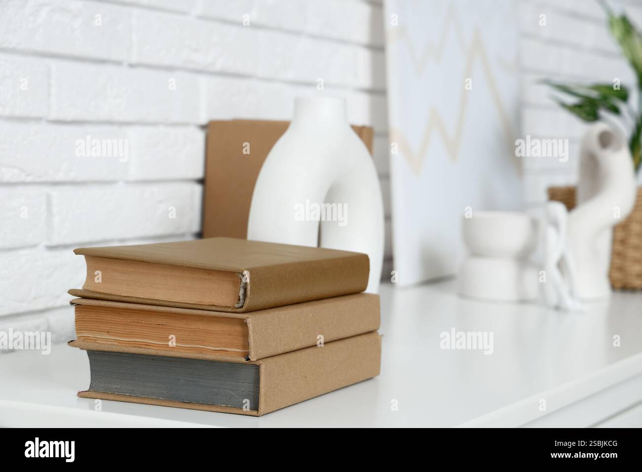Stack of old books and vases on chest of drawers near white brick wall ...