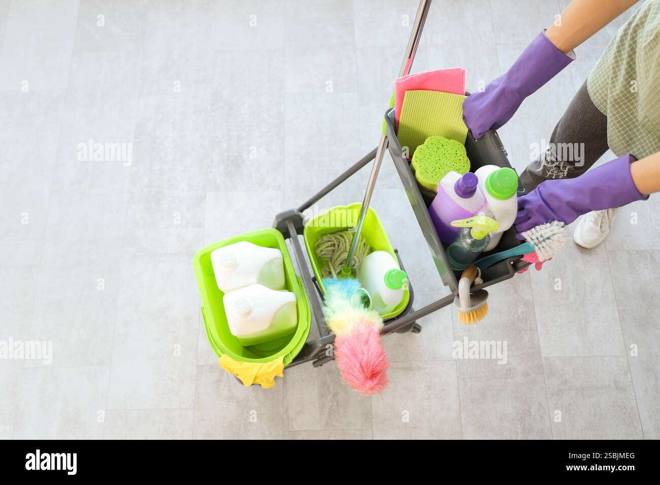 Female janitor with trolley of cleaning supplies in room, top view ...