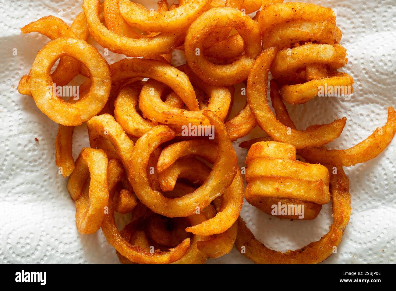 Seasoned spicy curly fries, freshly fried, on kitchen paper towel ...
