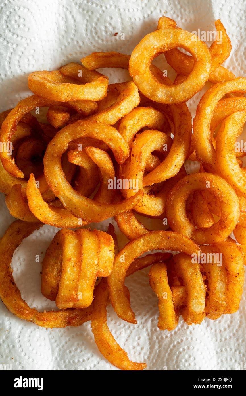 Seasoned spicy curly fries, freshly fried, on kitchen paper towel ...
