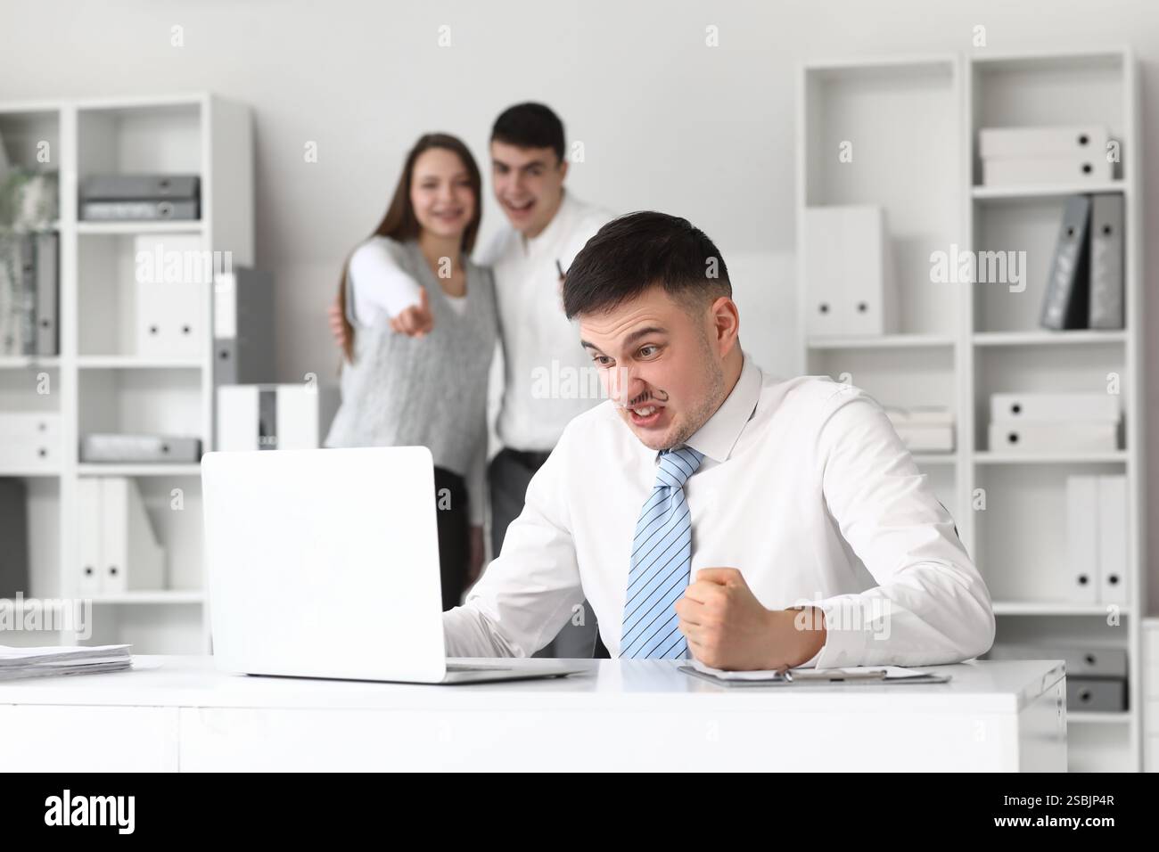 Angry young man with drawn mustache and his colleagues in office. April ...