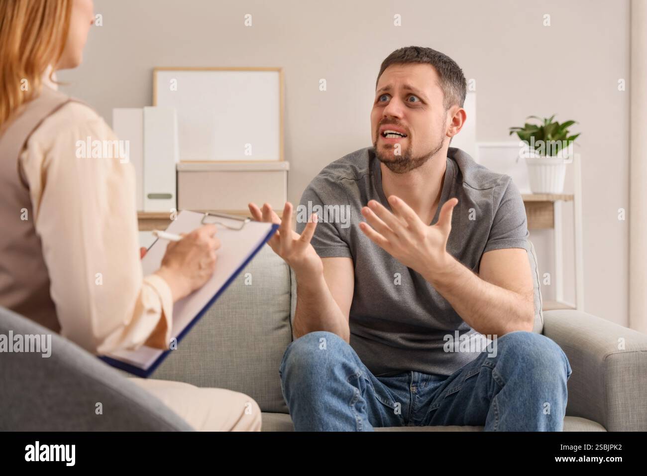 Male drug addict talking to psychologist on sofa in office Stock Photo ...